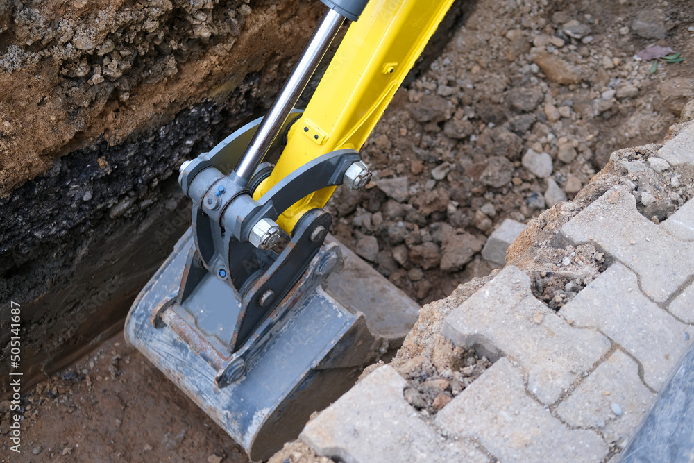 excavator bucket digs earth in trench on street, concept of repairing ...