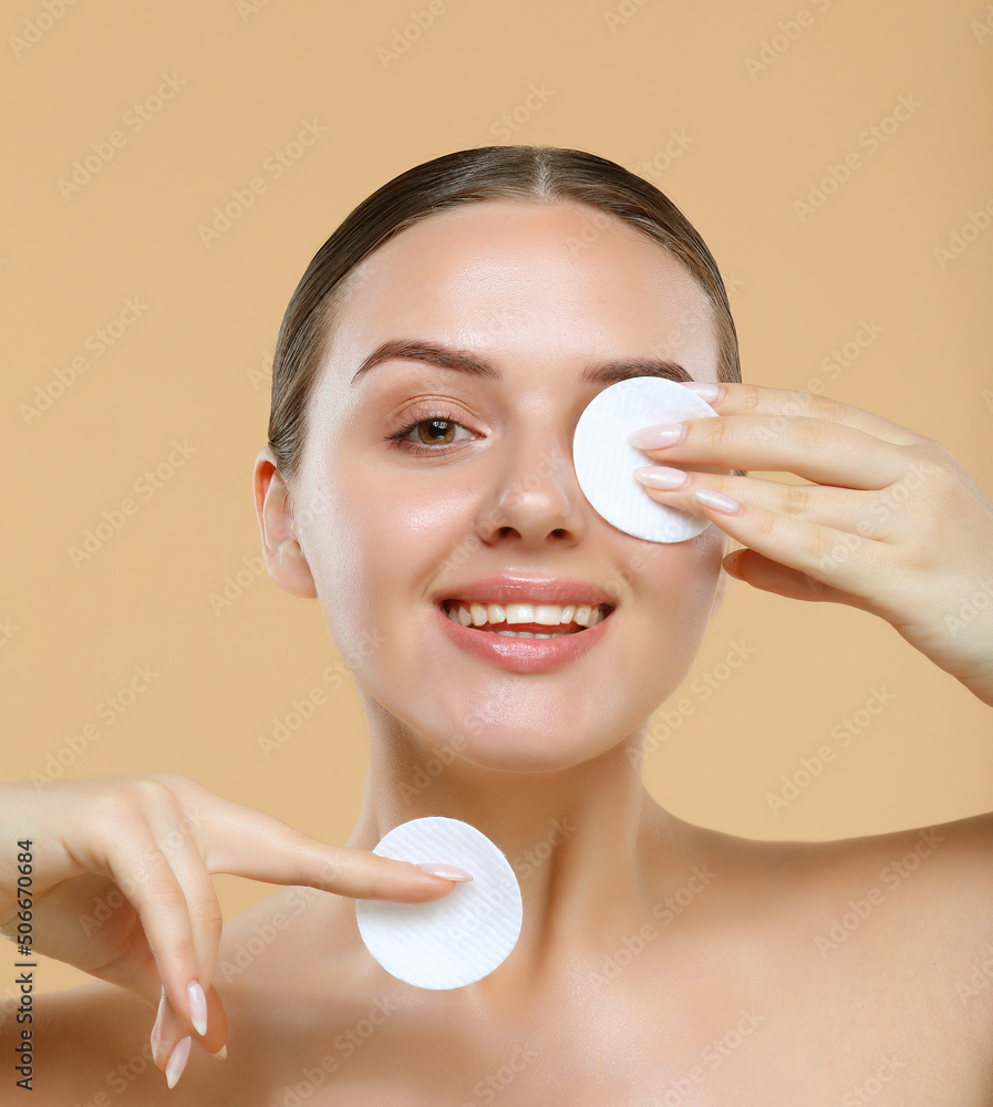 Attractive young female cleansing face with a cotton pad over beige ...