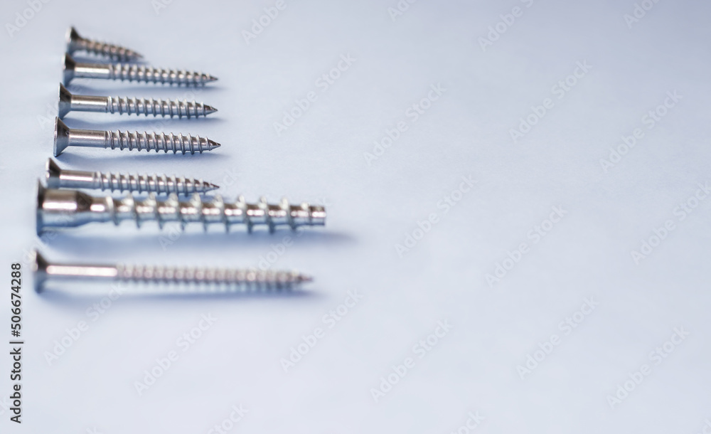 screw different sizes in a row on light blue background. Stainless bolt ...