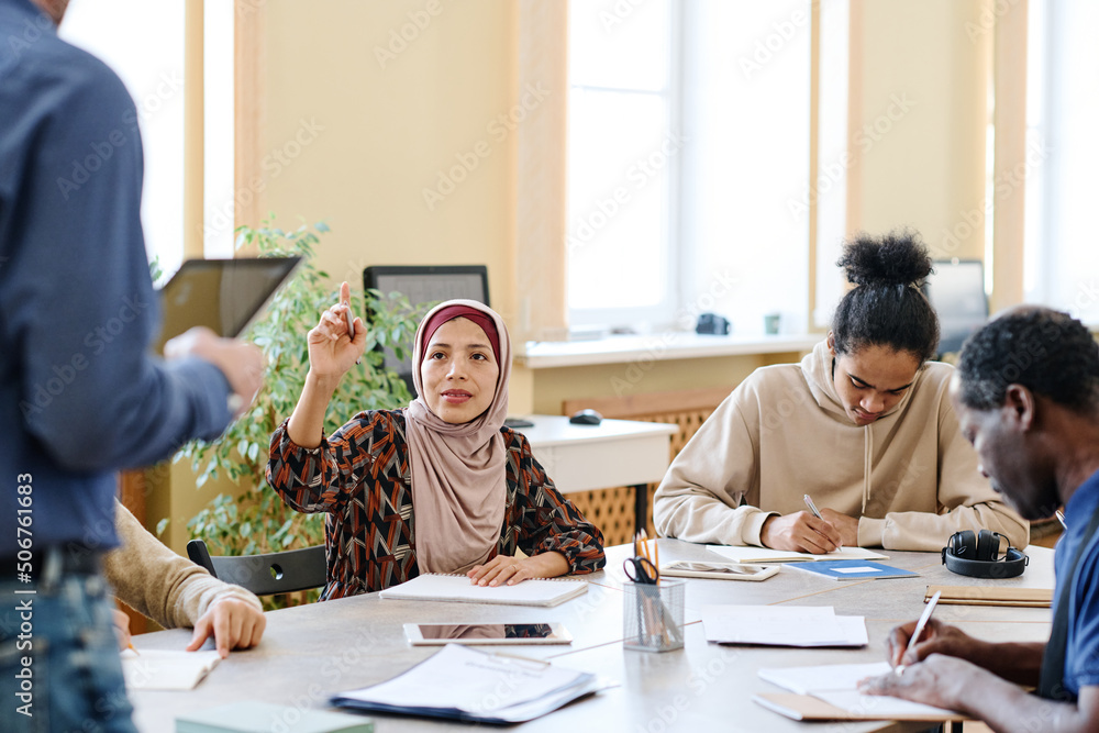 Muslim woman attending language lessons for immigrants raising hand to ...