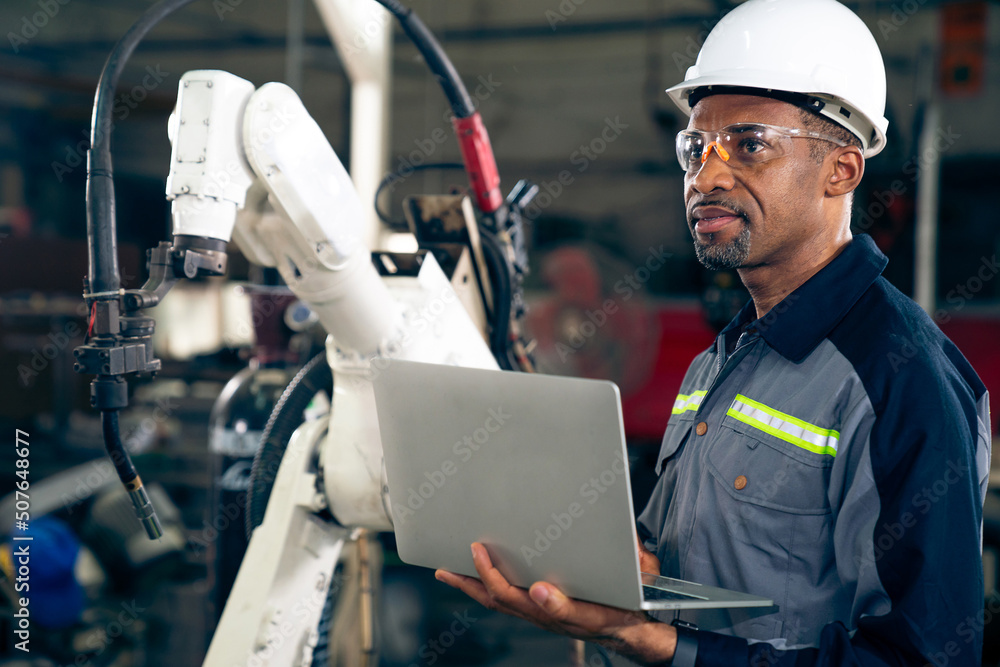 African American factory worker working with adept robotic arm in a ...