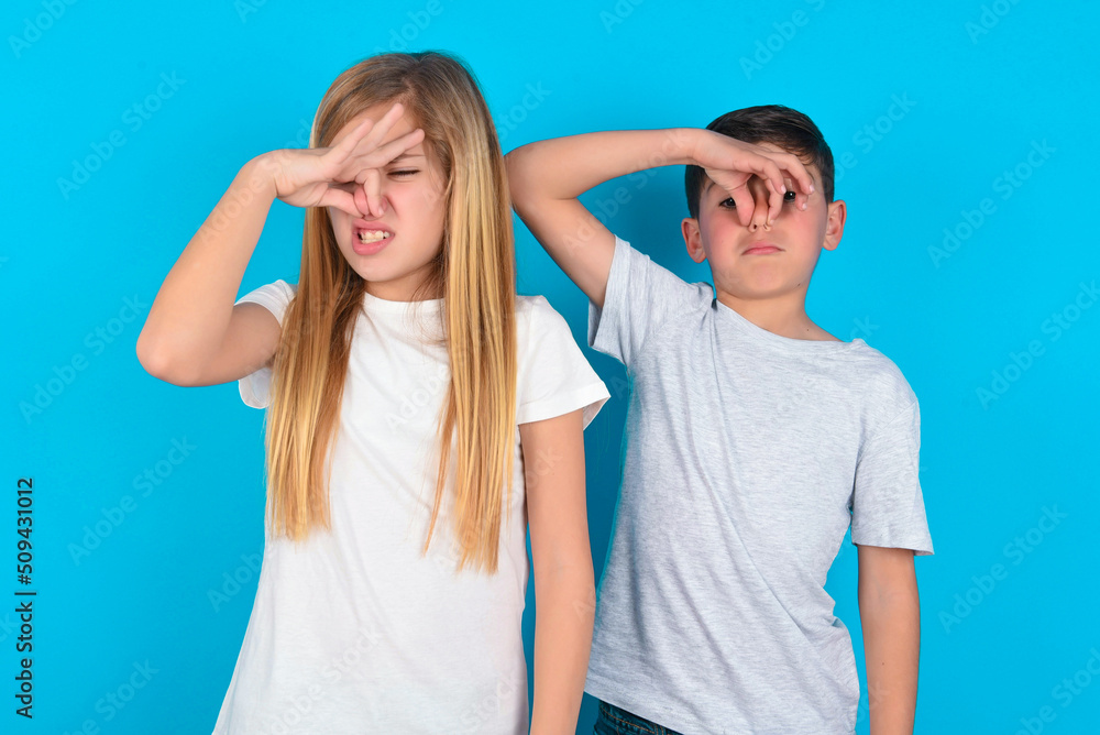 Displeased two kids boy and girl standing over blue studio background ...