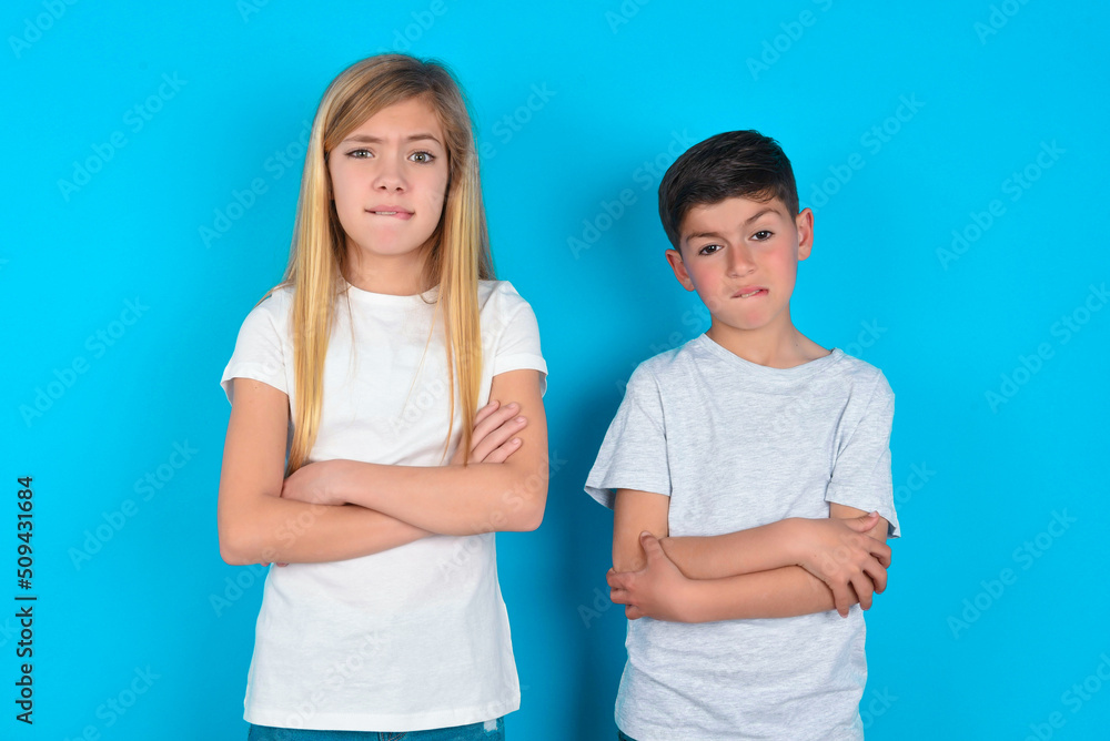 two kids boy and girl standing over blue studio background bitting his ...