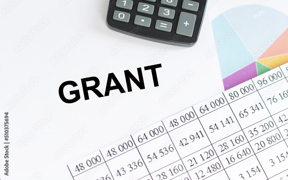 GRANT text on a notepad on the table among reports and a calculator, a ...