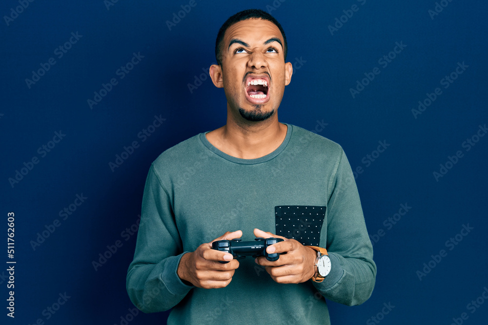 Young african american man playing video game holding controller angry ...