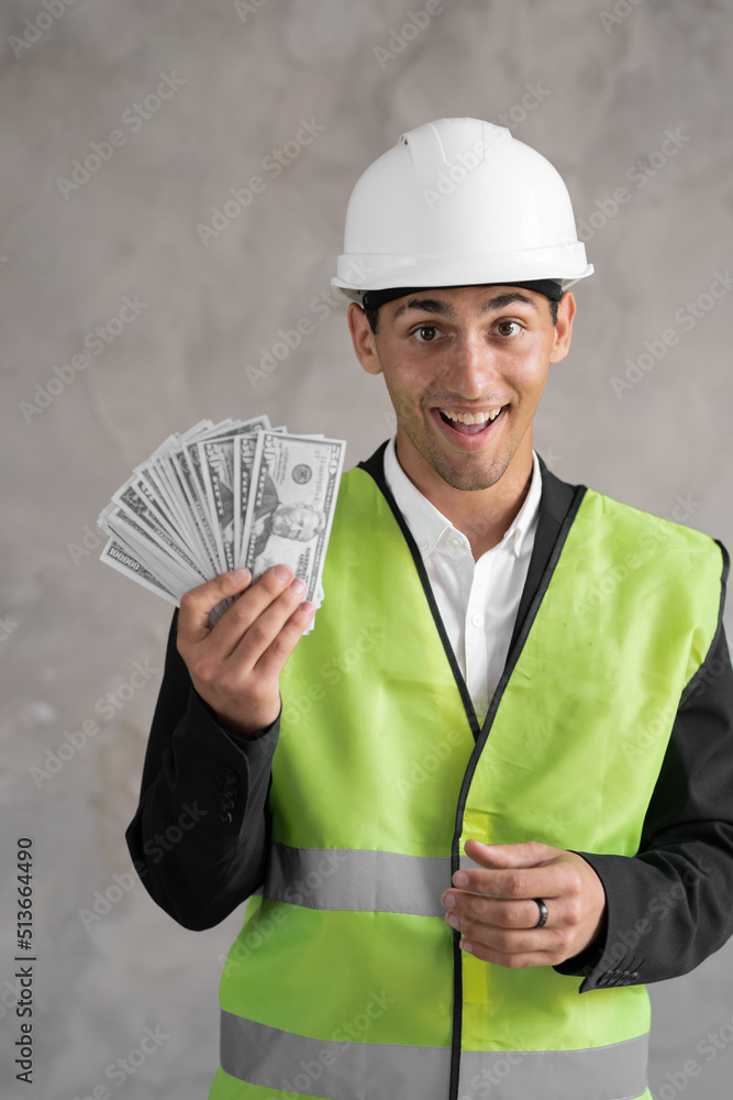 Young arabic builder man engineer wearing safety helmet holding money ...