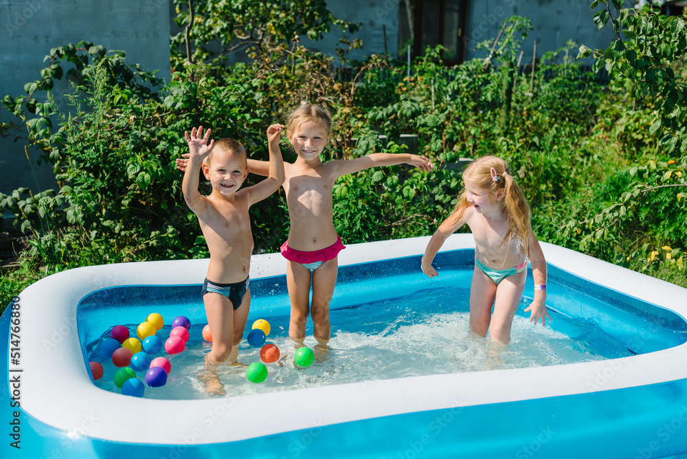 Three happy friends are splashing in an inflatable pool in the garden. Concept of summer season ...