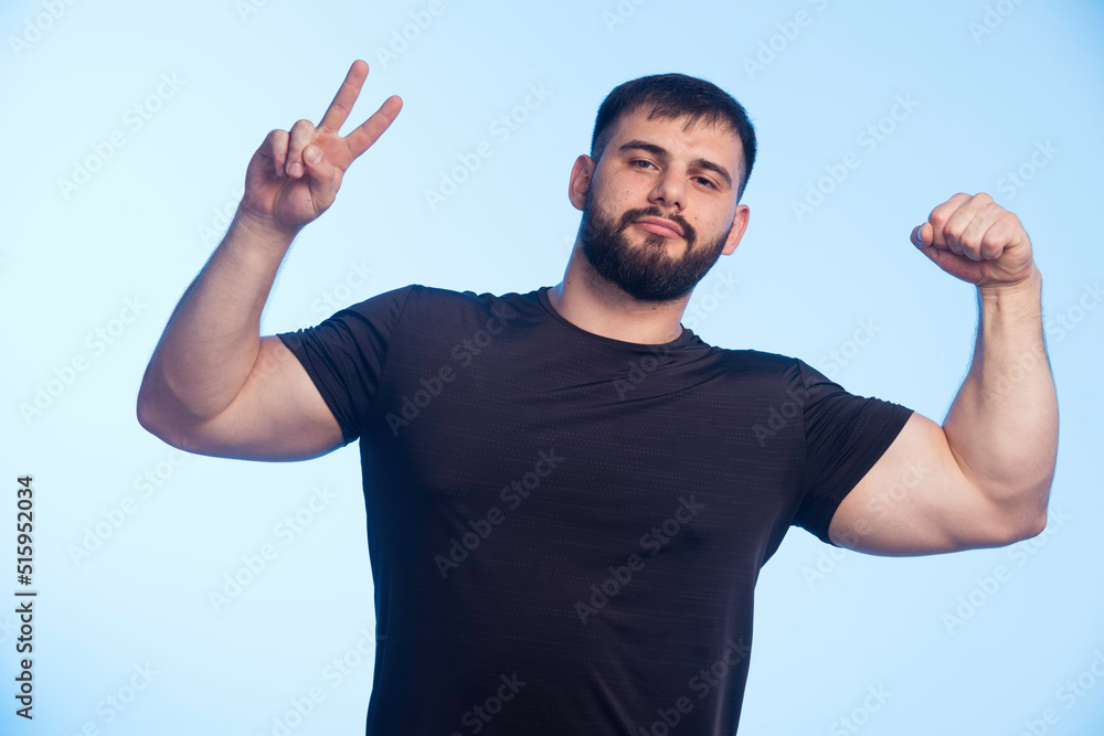 Sportive man in black shirt showing his muscles and making peace sign ...
