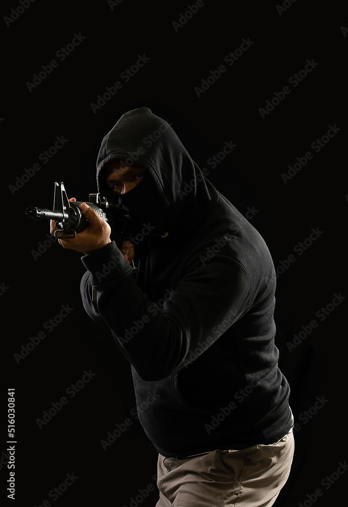 Portrait of a terrorist wearing a black hoodie holding a m16 rifle on a ...