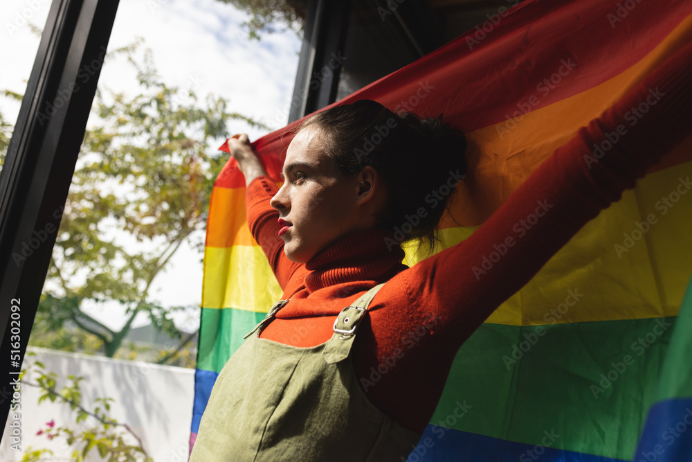 Image of caucasian non-binary trans woman holding rainbow flag and ...