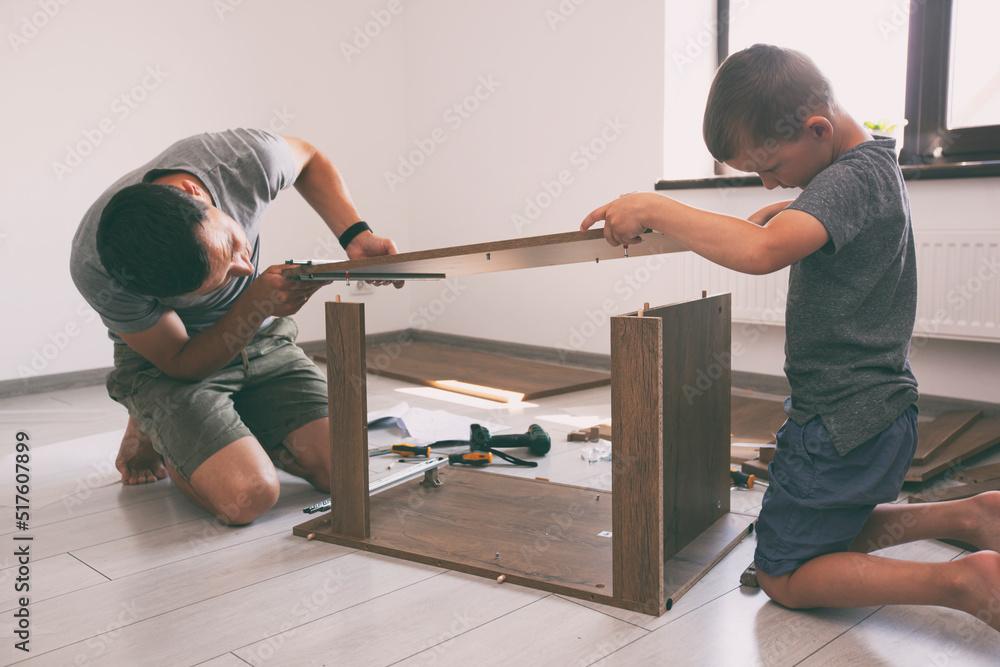 Father and son assembling the desk together and father teaches his son ...