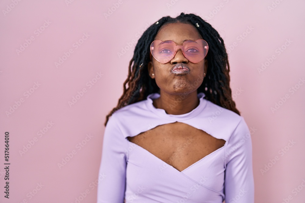 African woman with braided hair standing over pink background puffing ...