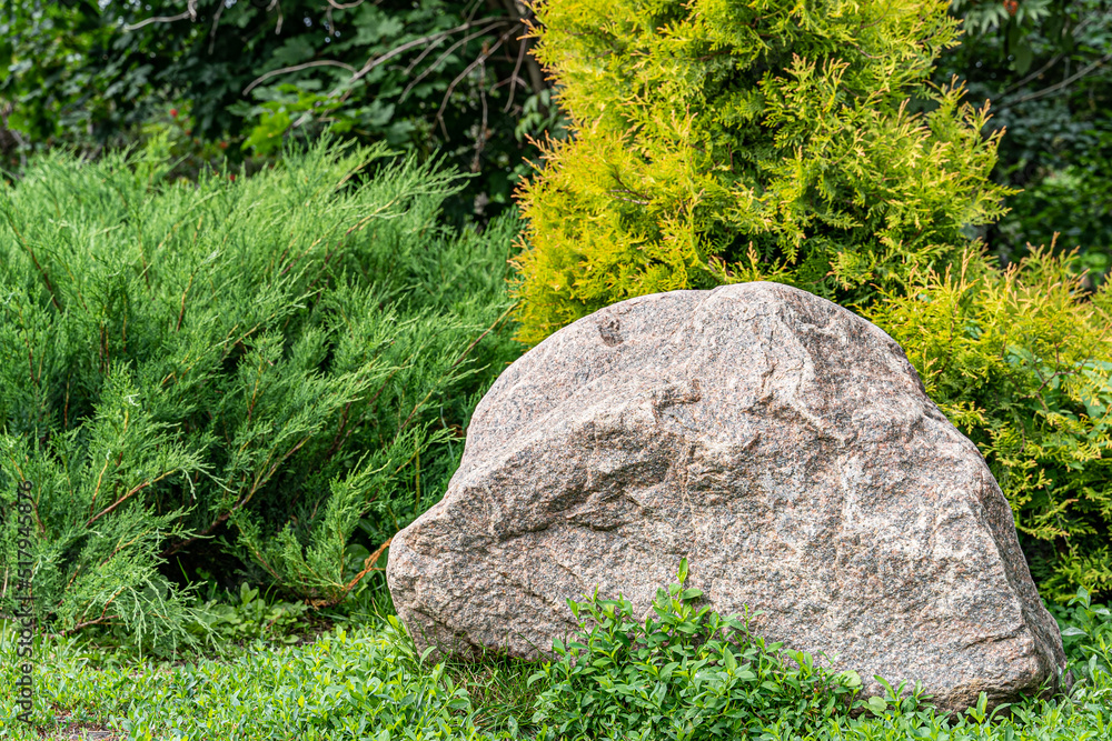 A huge granite stone boulder on a grass lawn against the background ...