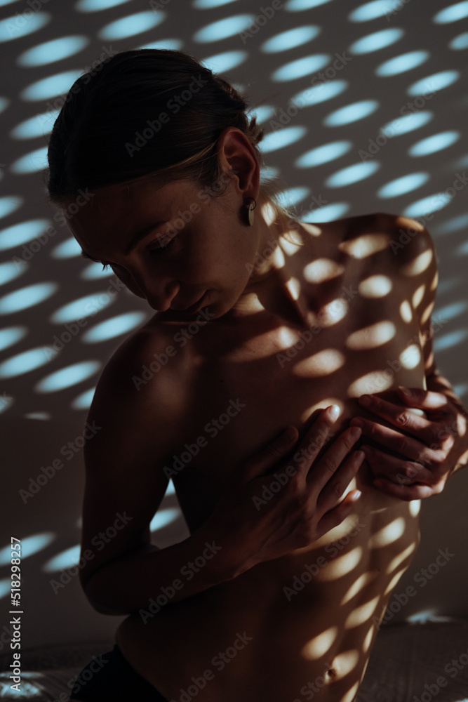 Portrait of a beautiful nude woman posing under a patterned shadow. Beauty of female body ...