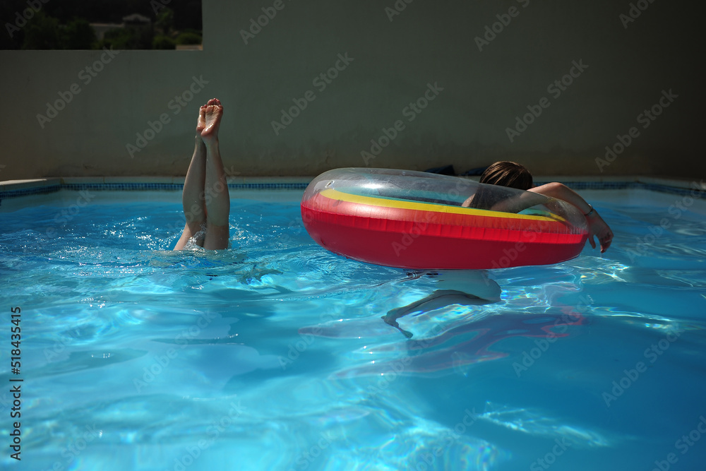 Two teenage girls play in a swimming pool with a rainbow pool float ...