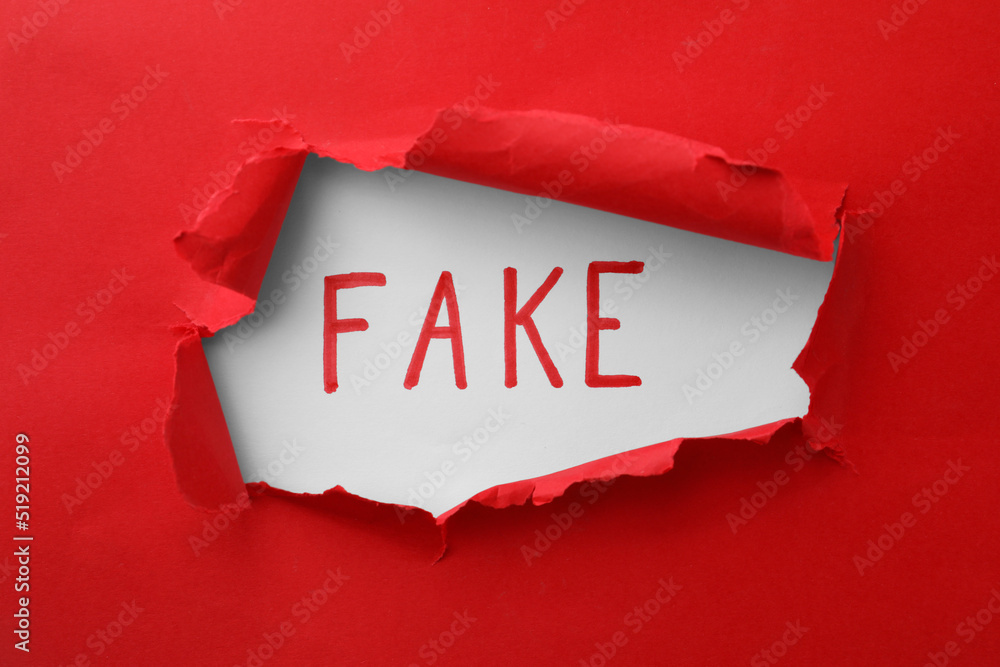 Word Fake written on white background, view through hole in red torn ...