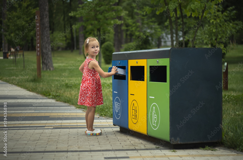 Cute little girl throw paper garbage into blue container in a park ...