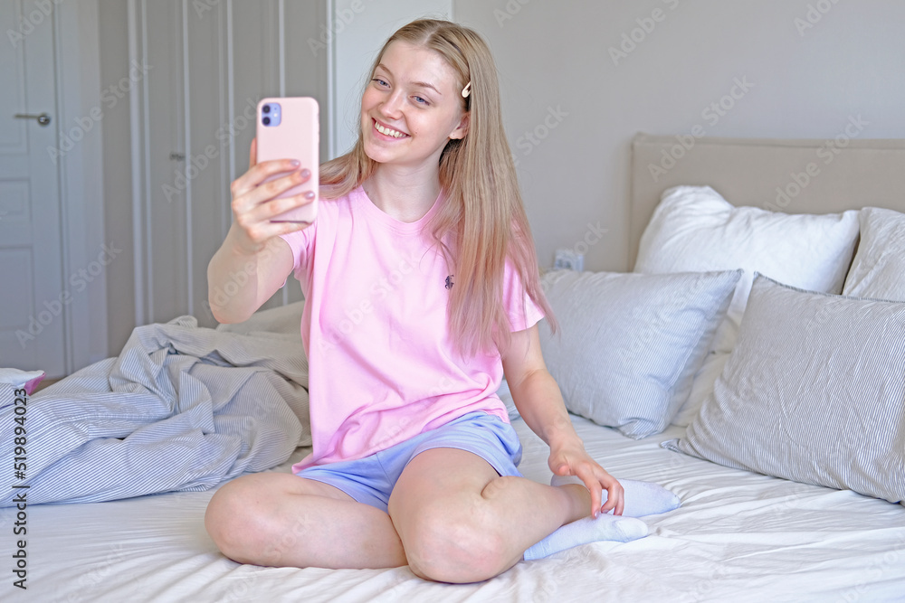 Cute girl 15-18 years old sitting on the bed makes a selfie. Stock Photo | Adobe Stock