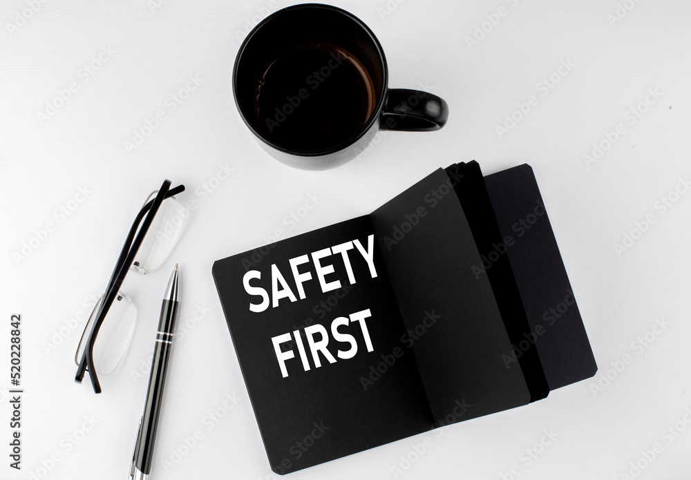 SAFETY FIRST written text in small black notebook with coffee , pen and ...