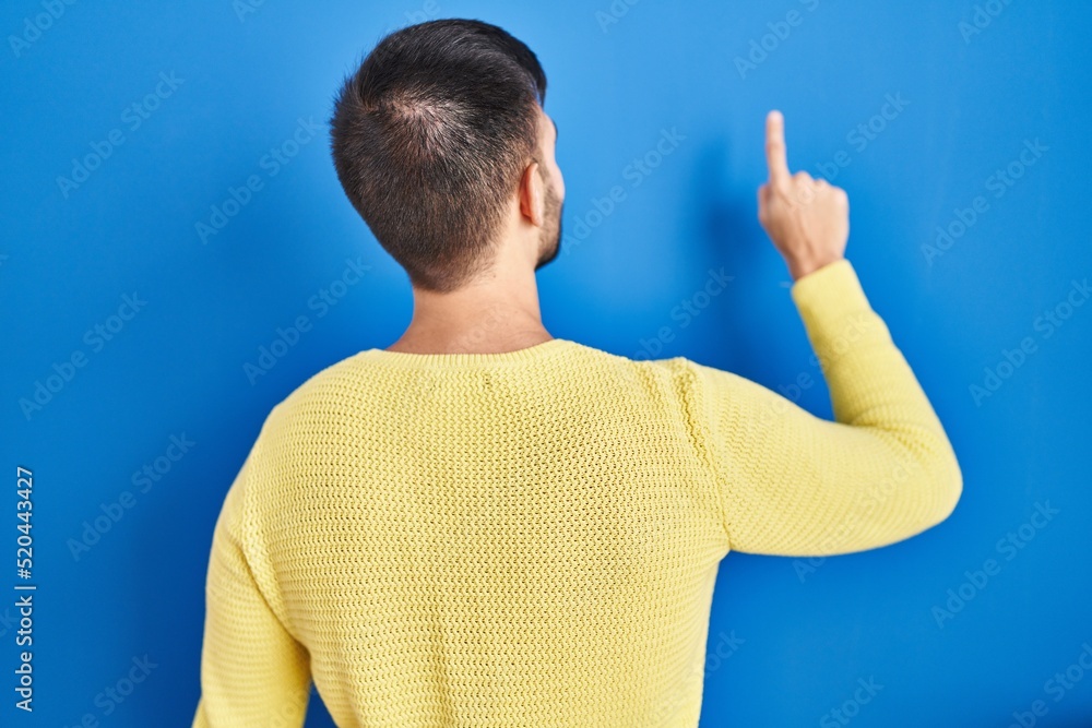 Hispanic man standing over blue background posing backwards pointing ...