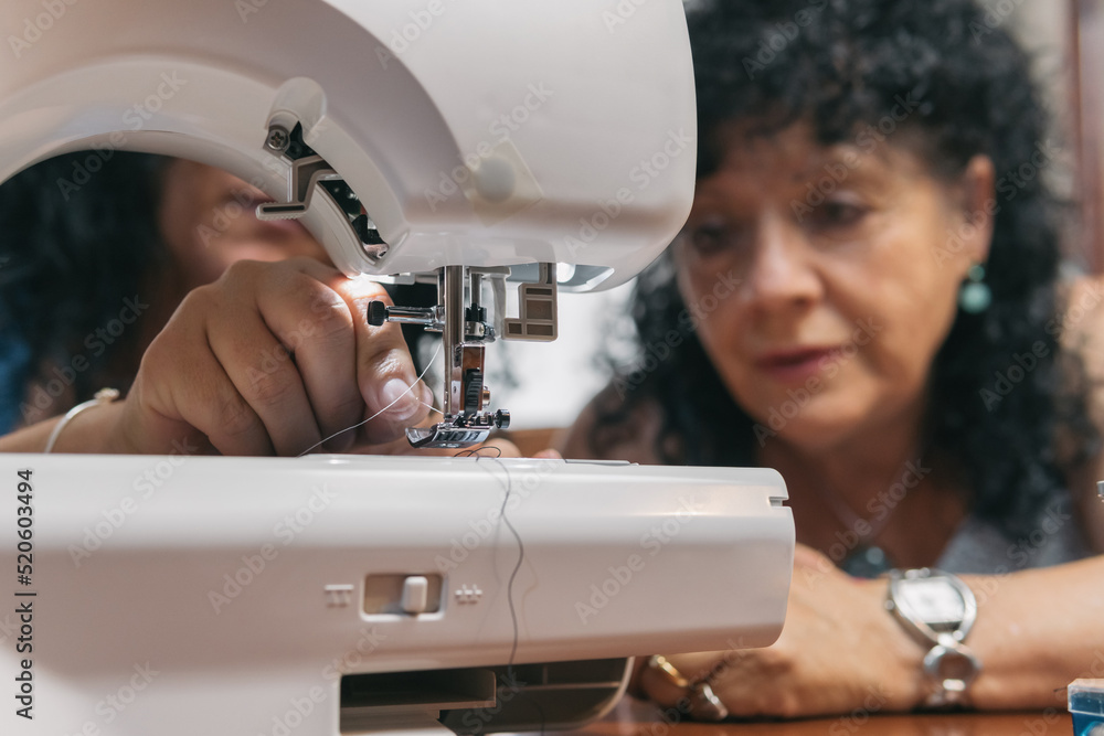 Older woman watching how her daughter performs the sewing and tailoring ...