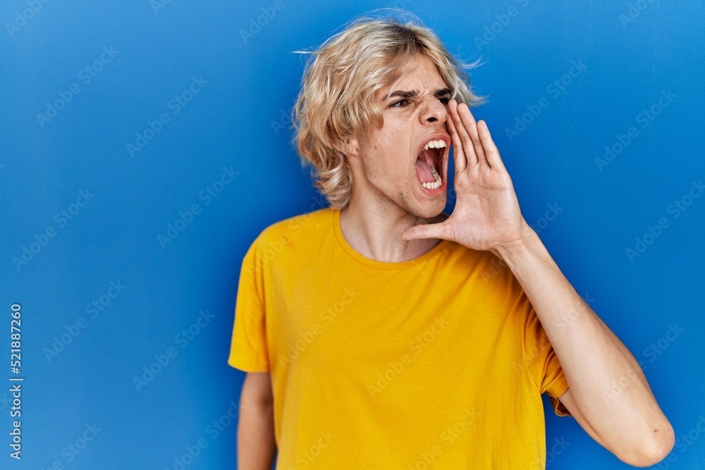 Young modern man standing over blue background shouting and screaming ...