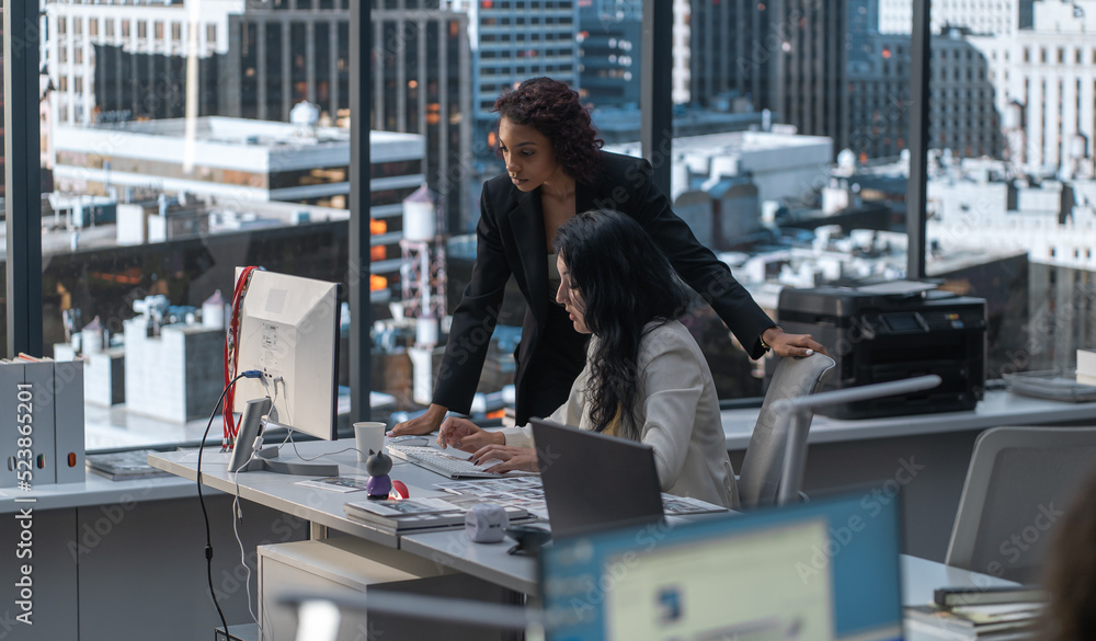Two diverse female office employees working on something together in th ...