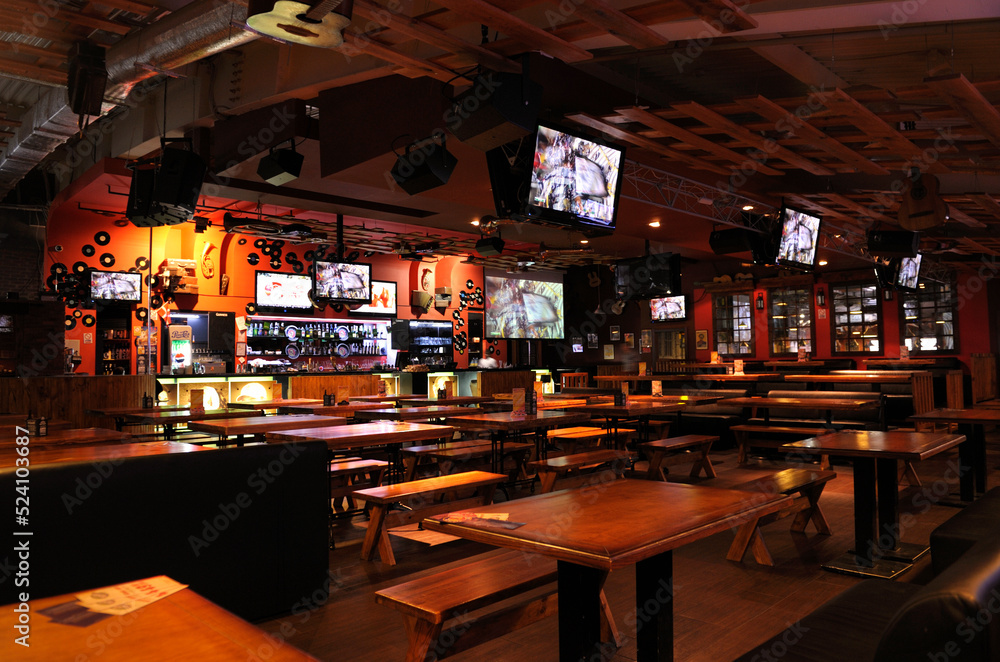 Interior of an empty sport pub, wooden tables, screens, bar counter ...