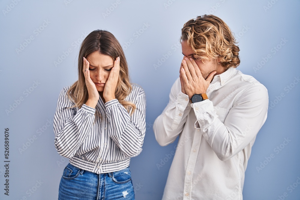 Young couple standing over blue background with sad expression covering ...