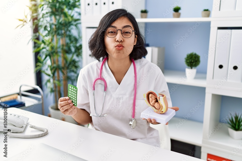 Young hispanic doctor woman holding anatomical model of uterus with ...