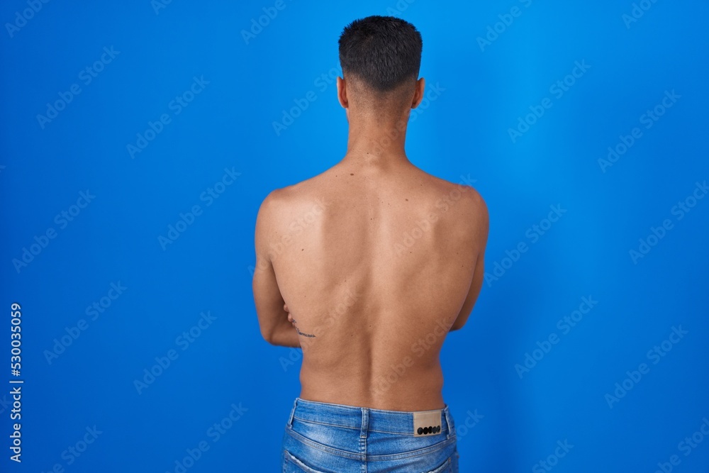 Young hispanic man standing shirtless over blue background standing ...