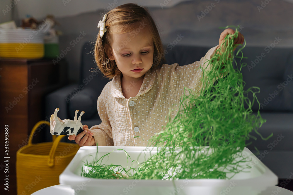 A little girl playing with farm animals in sensory bin with green ...