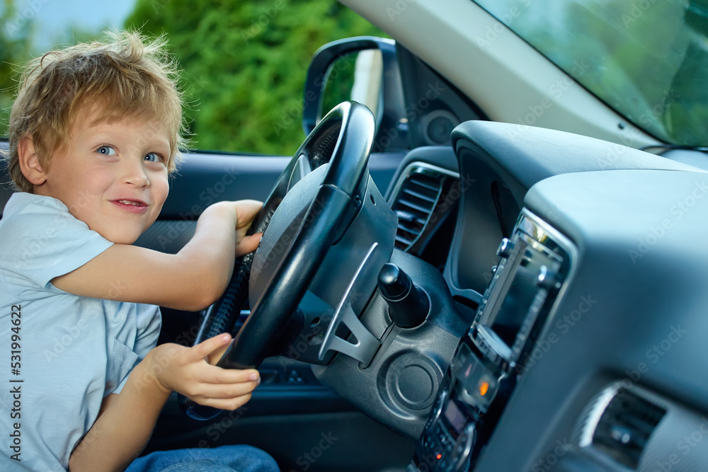 Funny kid twists the steering wheel of a car while playing rally racer ...