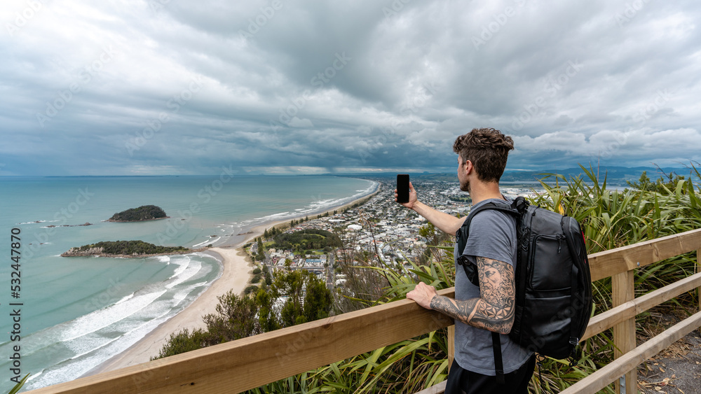 Stock-Foto „Man taking a photo with mobile of Mount Maunganui from the ...