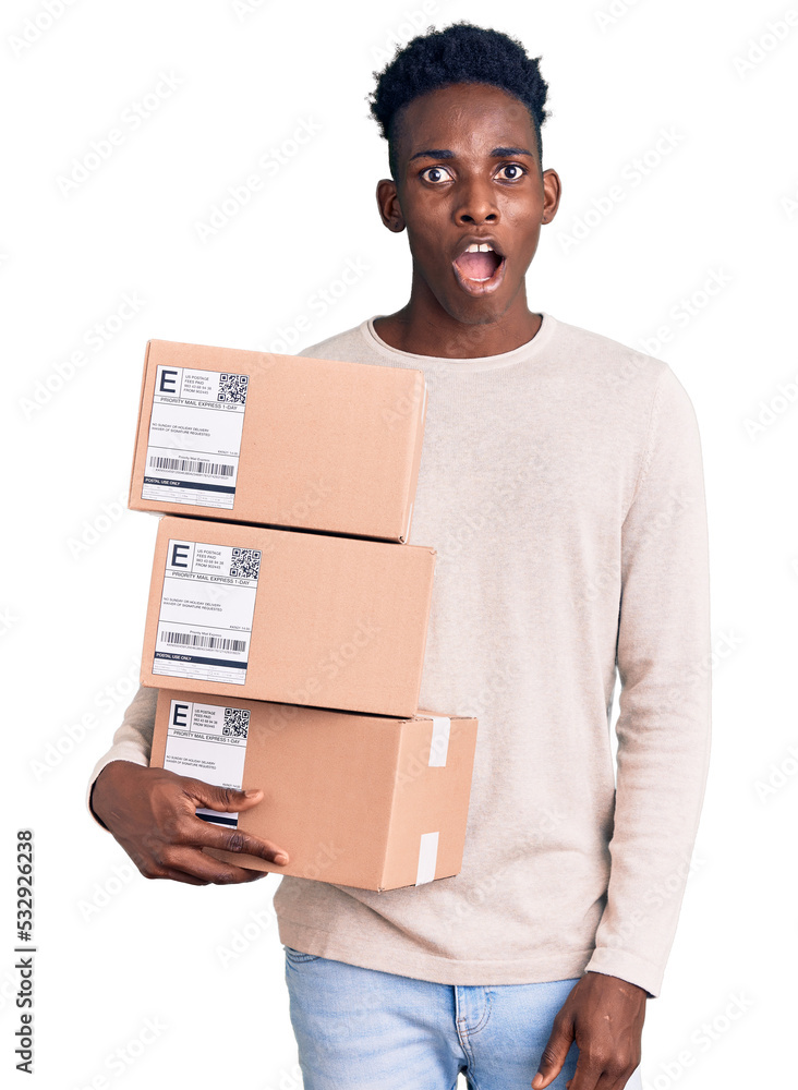 Young african american man holding delivery package scared and amazed ...