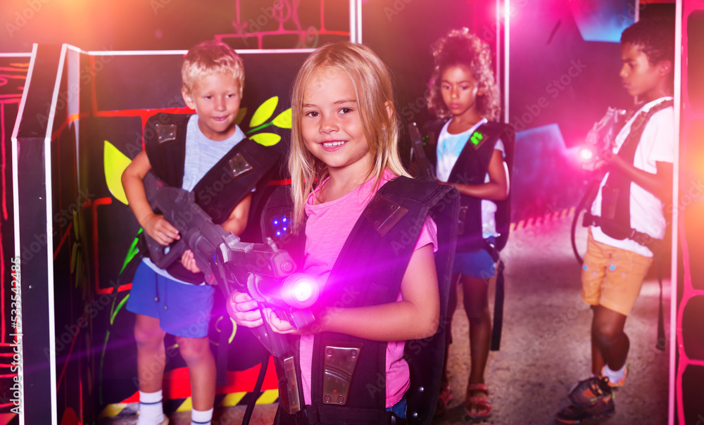 Cute preteen girl with laser pistol playing laser tag with friends on ...