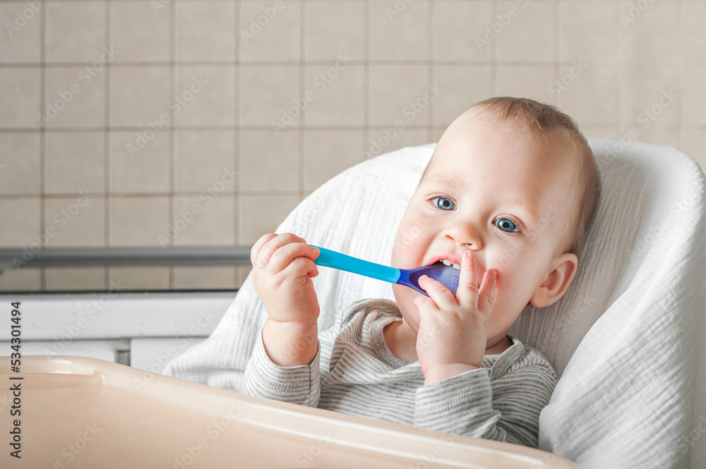 11 month old baby with spoon on high chair. First baby food, pureed food, baby-led weaning, BLW ...