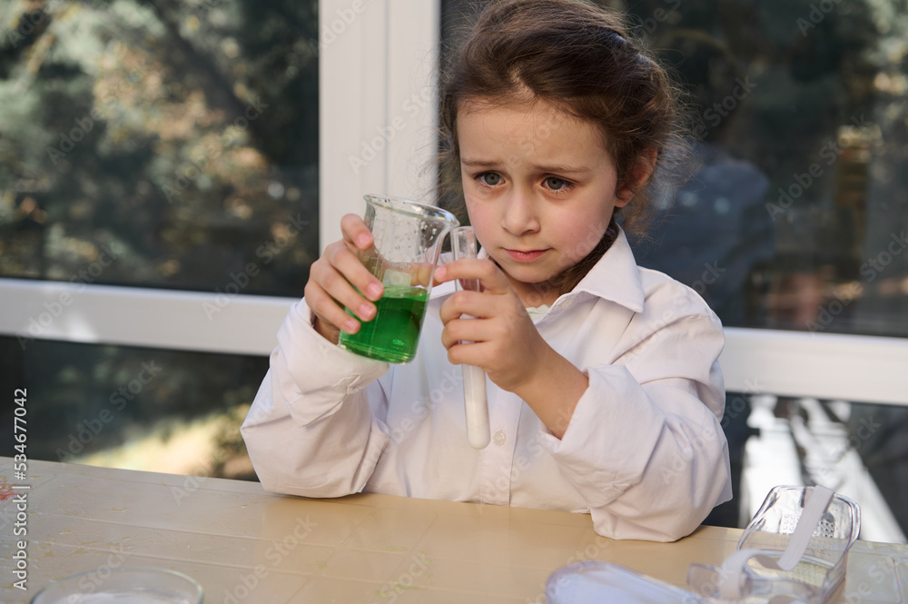 Caucasian little girl in white lab coat, conducts chemical experiment ...