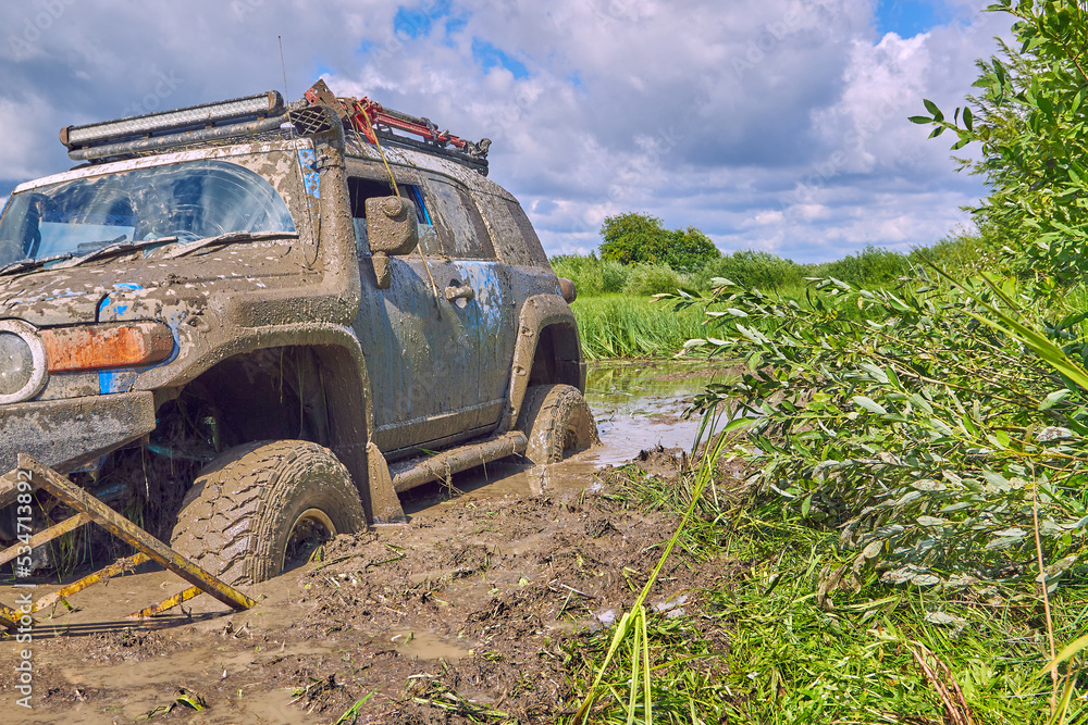 Off-road blue 4wd car is stuck in a muddy field against a beautiful sky ...