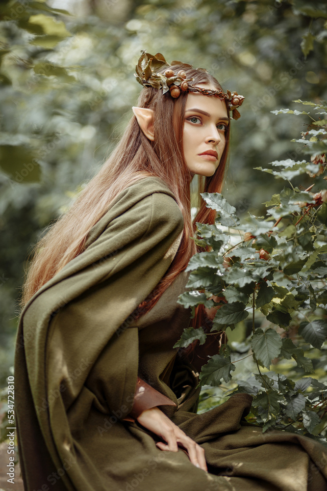 Elf girl dressed in a cape and with a wreath on her head in the forest. Fantasy elf from the ...