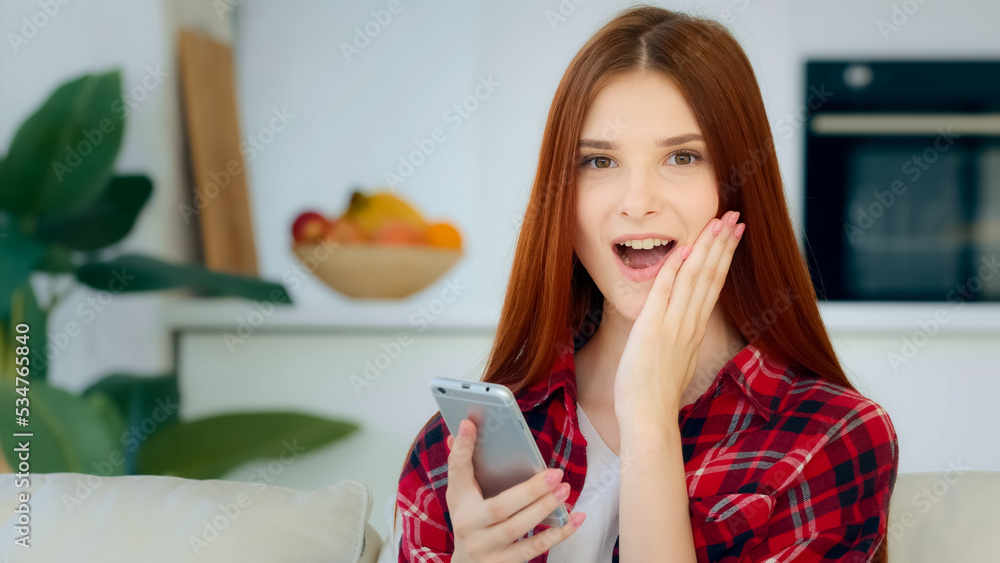 Amazed young user girl ginger student schoolgirl teenager use mobile app on phone shopping ...