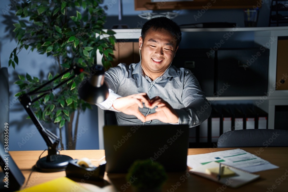 Young chinese man working using computer laptop at night smiling in ...