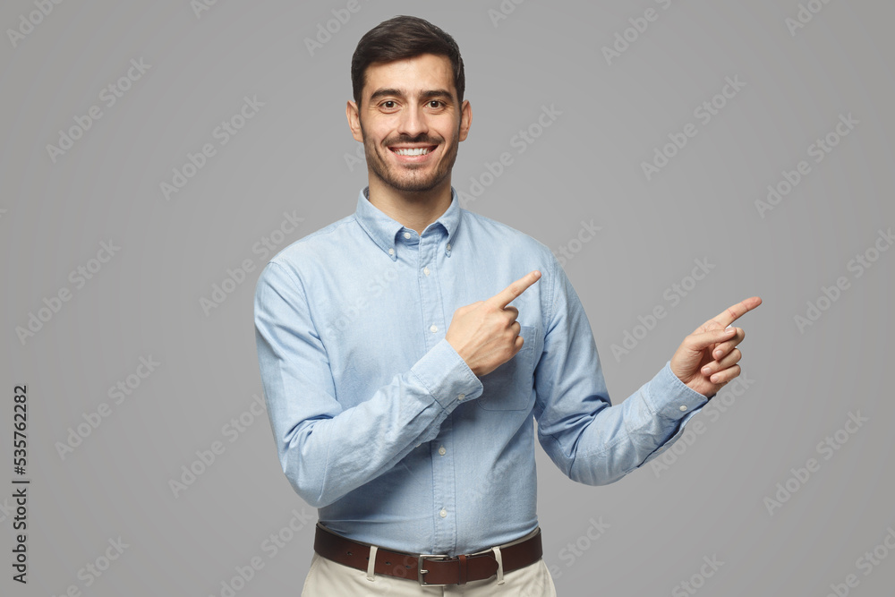 Smiling businessman pointing right with two hands looking at camera ...