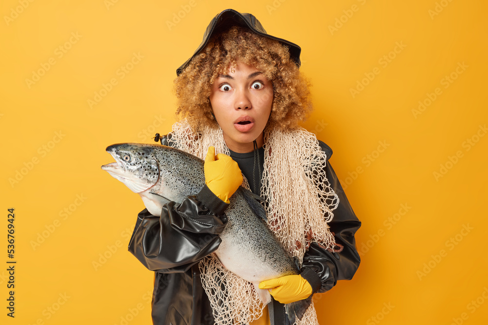 Scared frightened curly haired fisherwoman carries big salmon cannot ...