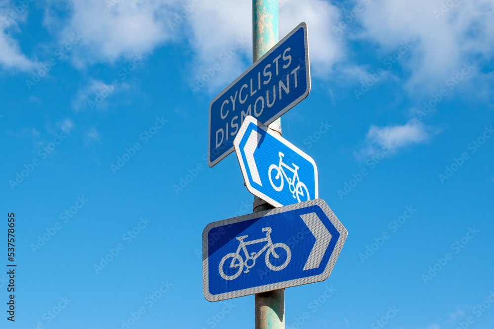 Cyclists dismount sign with blue cycle path signs pointing in opposite ...