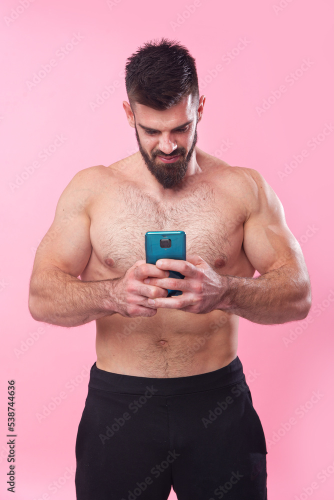 Shirtless strong bodybuilder talking on his cell, using a smartphone ...