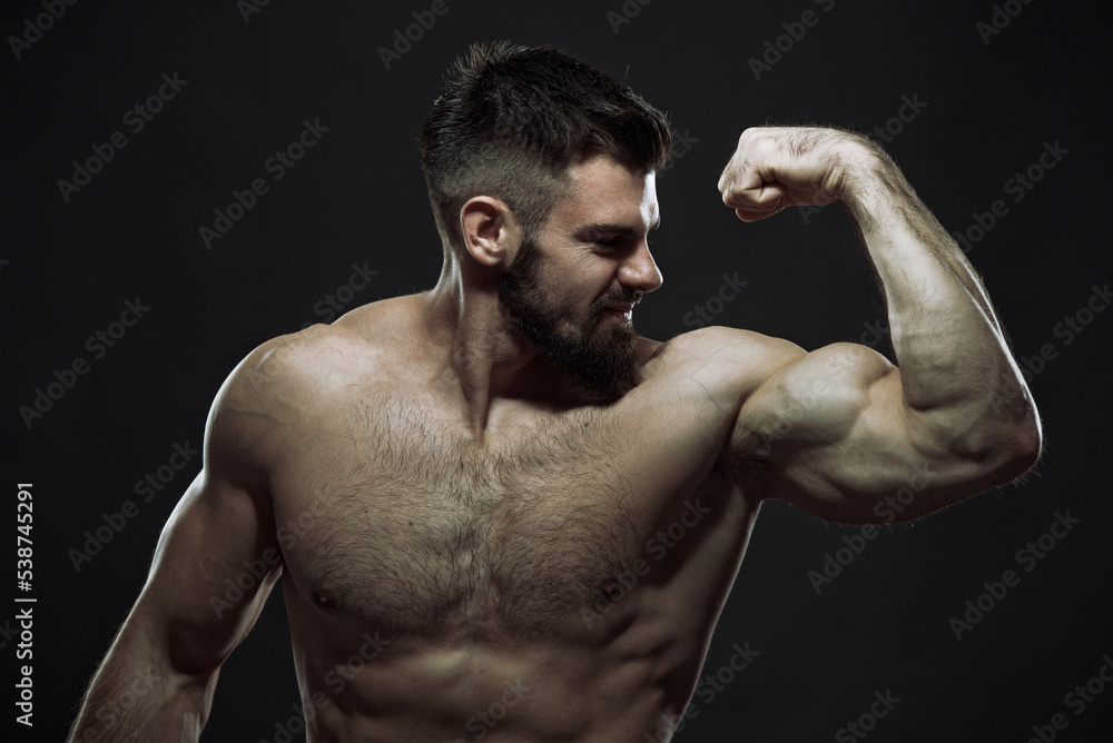 Strong shirtless man, a bodybuilder, flexing his biceps, showing off ...