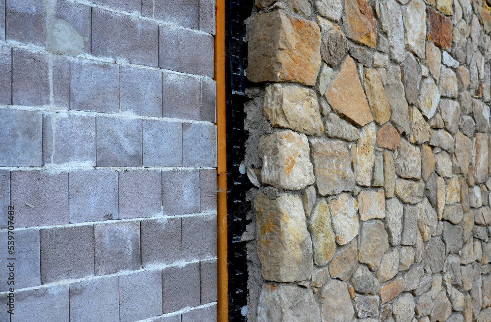 bricklayers tiling the house with sandstone stones. They connect stones ...