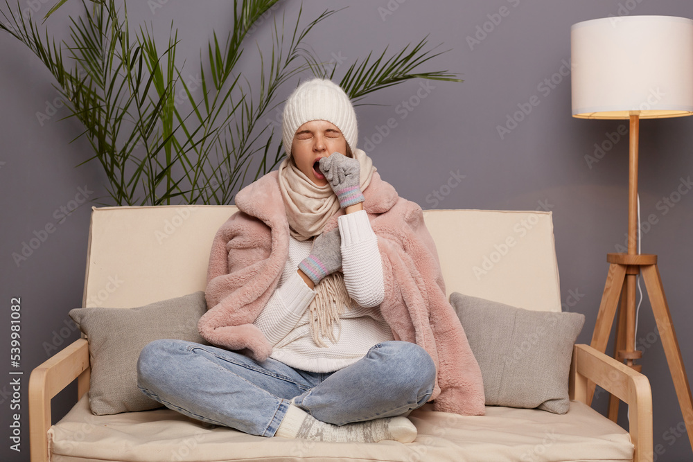 Full length portrait of sleepy woman posing in cold room sitting on the ...