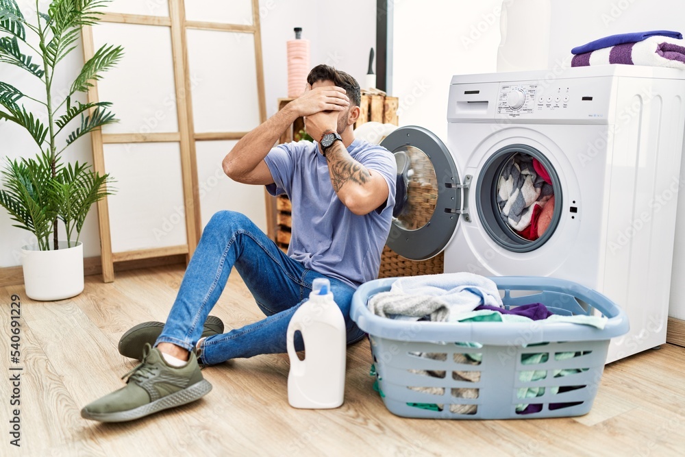 Young hispanic man putting dirty laundry into washing machine covering ...